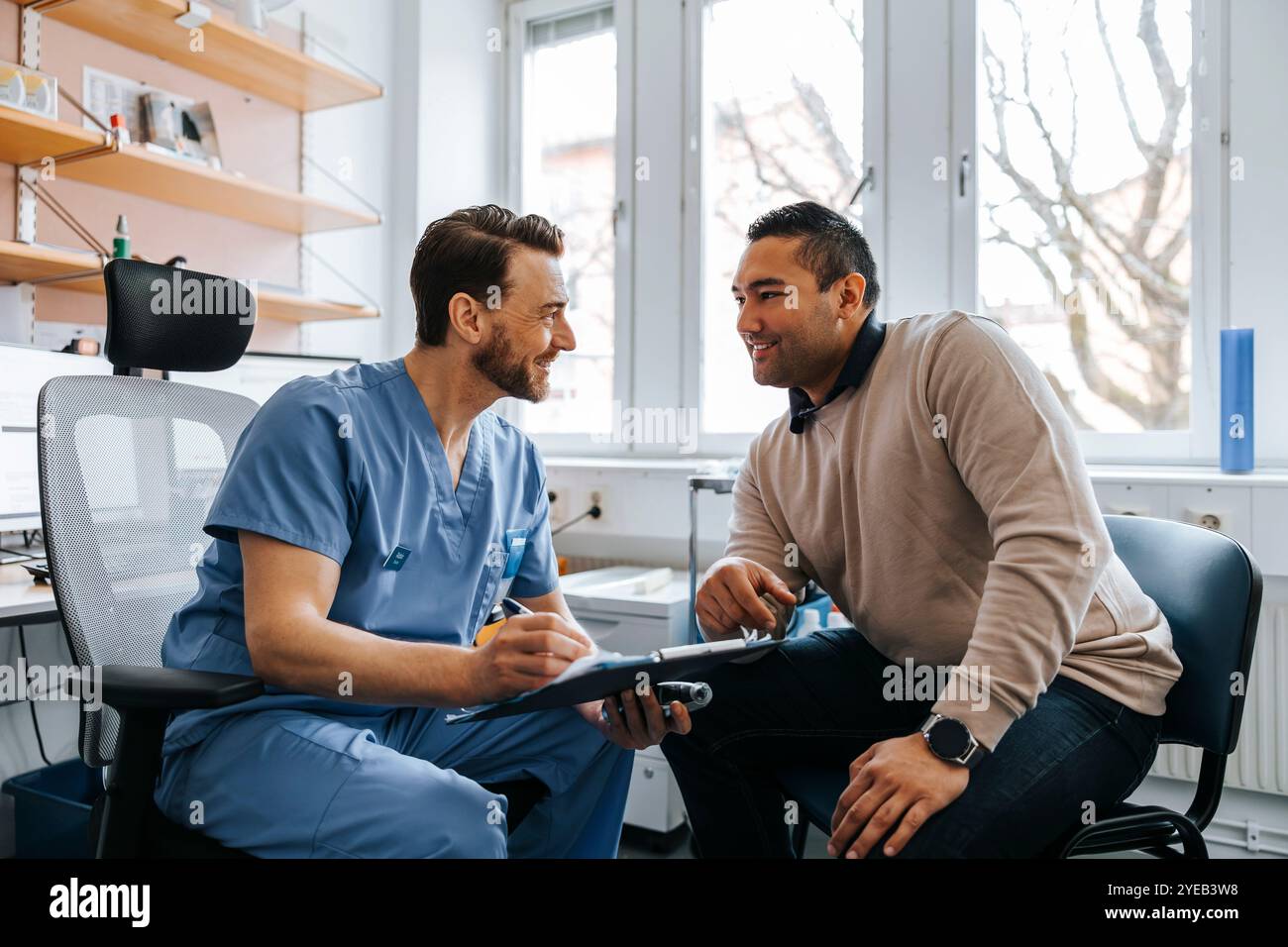 Happy male medical expert discussing reports with male patient during ...