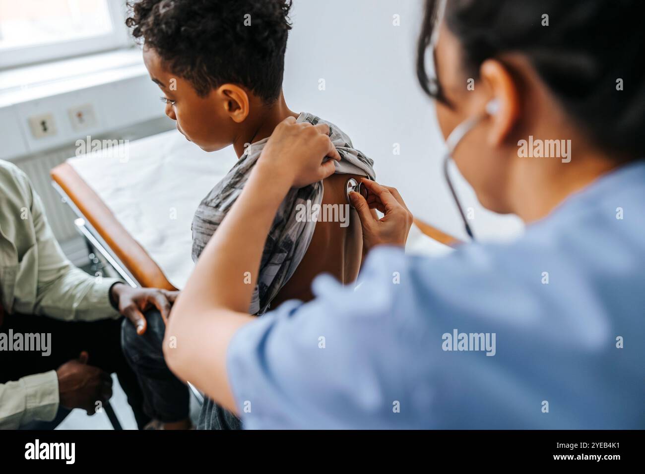 Female pediatrician examining boy's back with stethoscope in ...