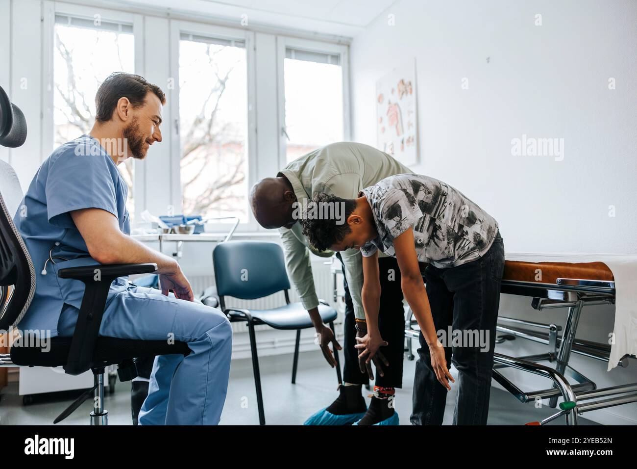 Side view of male doctor asking father and son to bend over while ...