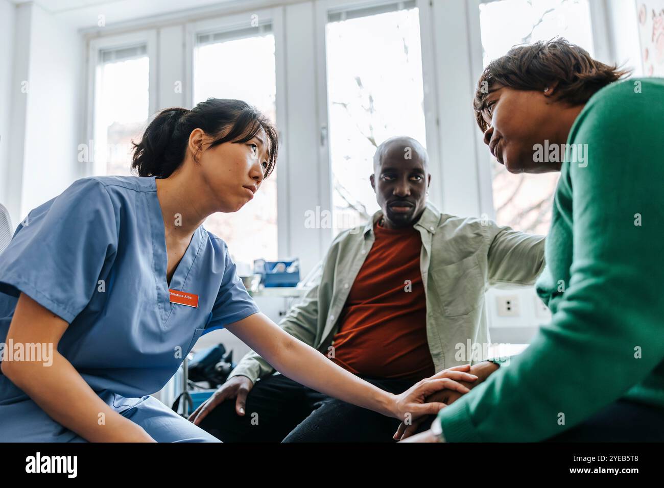 Sad female healthcare worker consoling senior patient sitting by son in ...