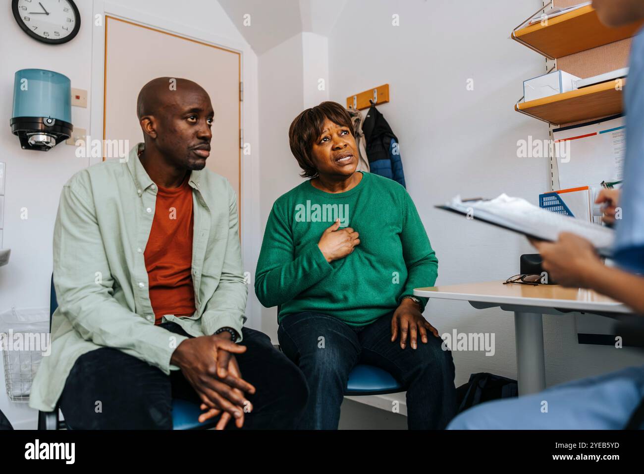 Senior woman explaining chest problems to doctor while sitting with son ...