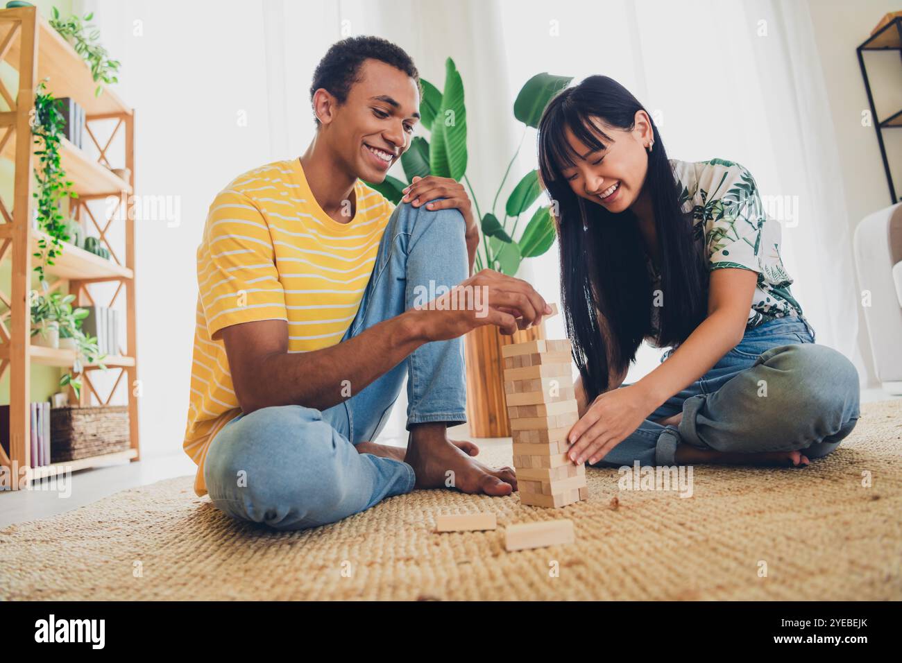 Photo of lovely cute positive multinational couple sit floor play jenga build tower pile stack ...