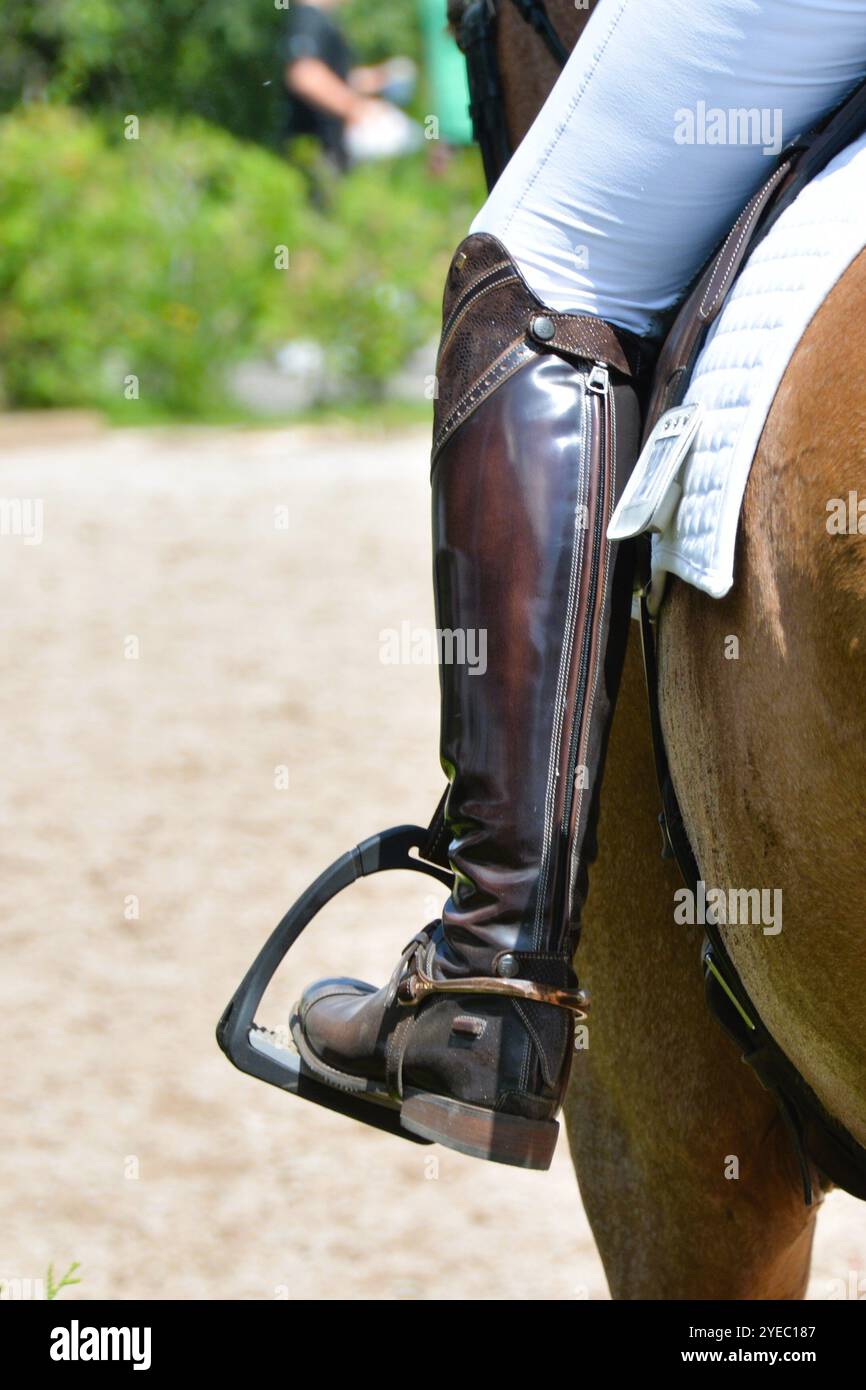 A closeup of the leg, boot, and stirrup of a dressage horseback rider ...
