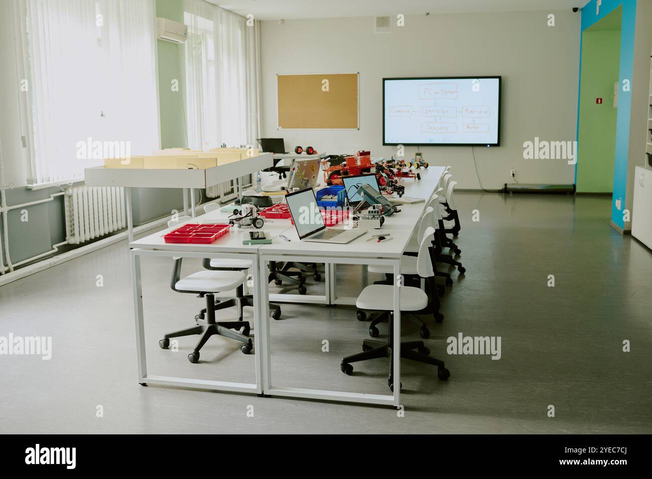 Empty classroom equipped with tables with electronic devices and robots ...