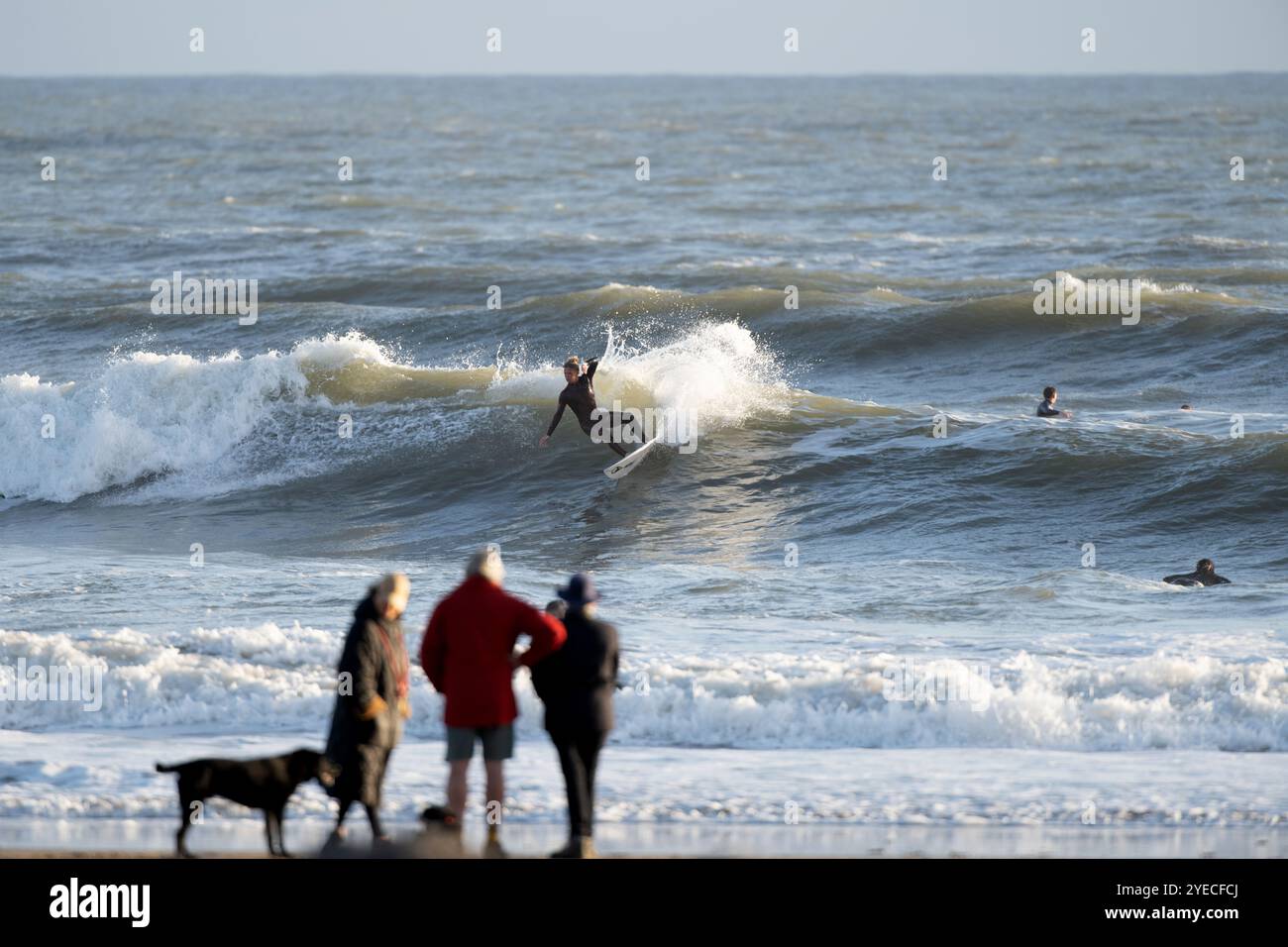 Surfer turns sending plume of spray into the air watched by passers by ...