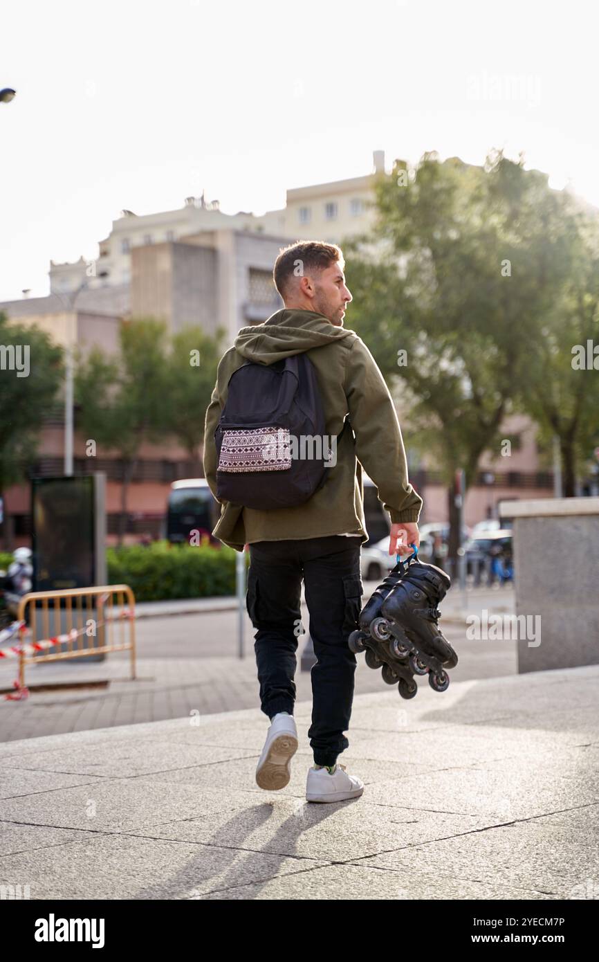 man walking down the street carrying his inline skates in his hand ...