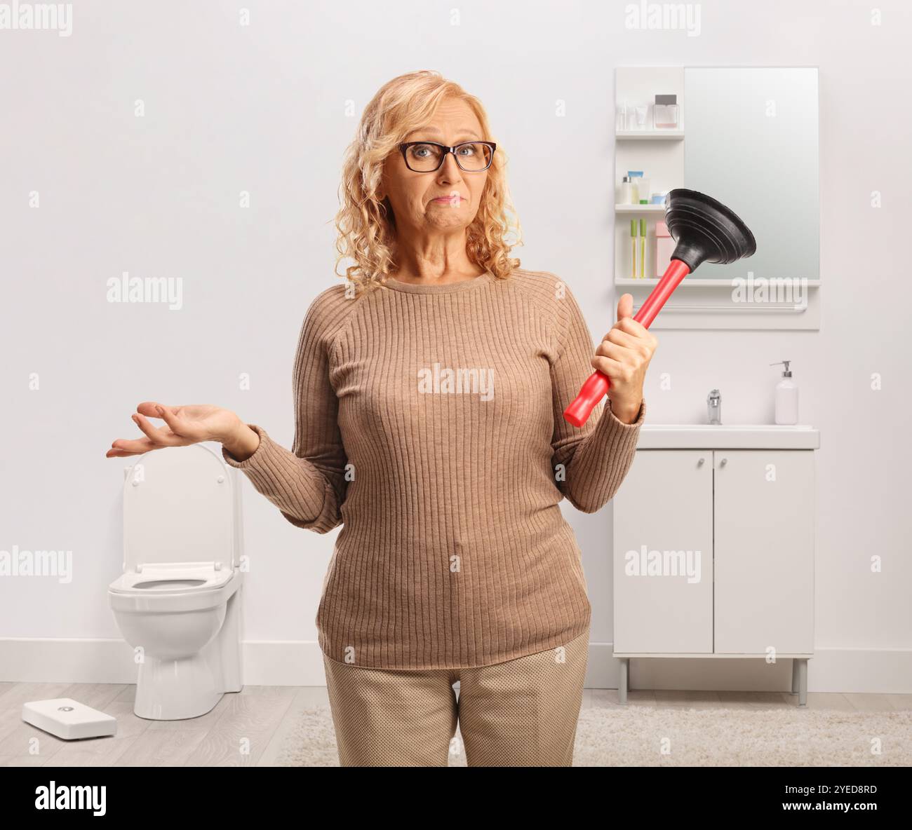 Confused mature woman holding a toilet plunger inside a bathroom Stock ...