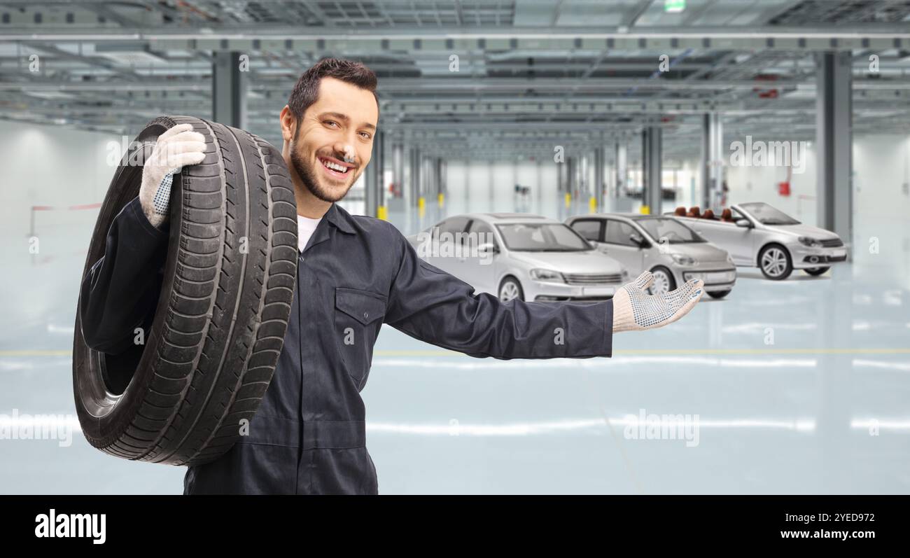 Auto mechanic with a tire gesturing welcome in a car garage Stock Photo ...