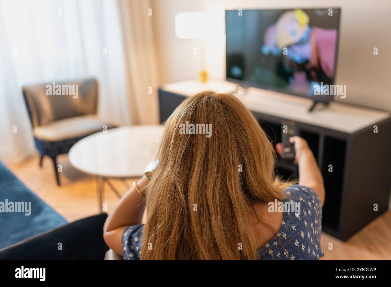 Woman in the living room changing the TV channel with the remote ...