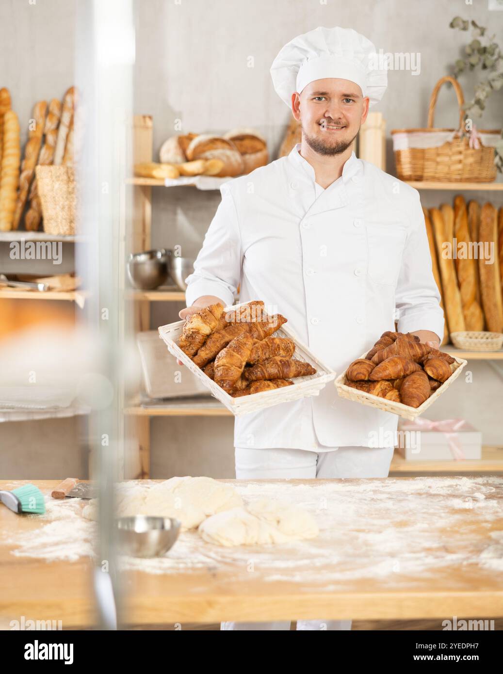 Baker in white uniform stands behind counter in small private bakery ...