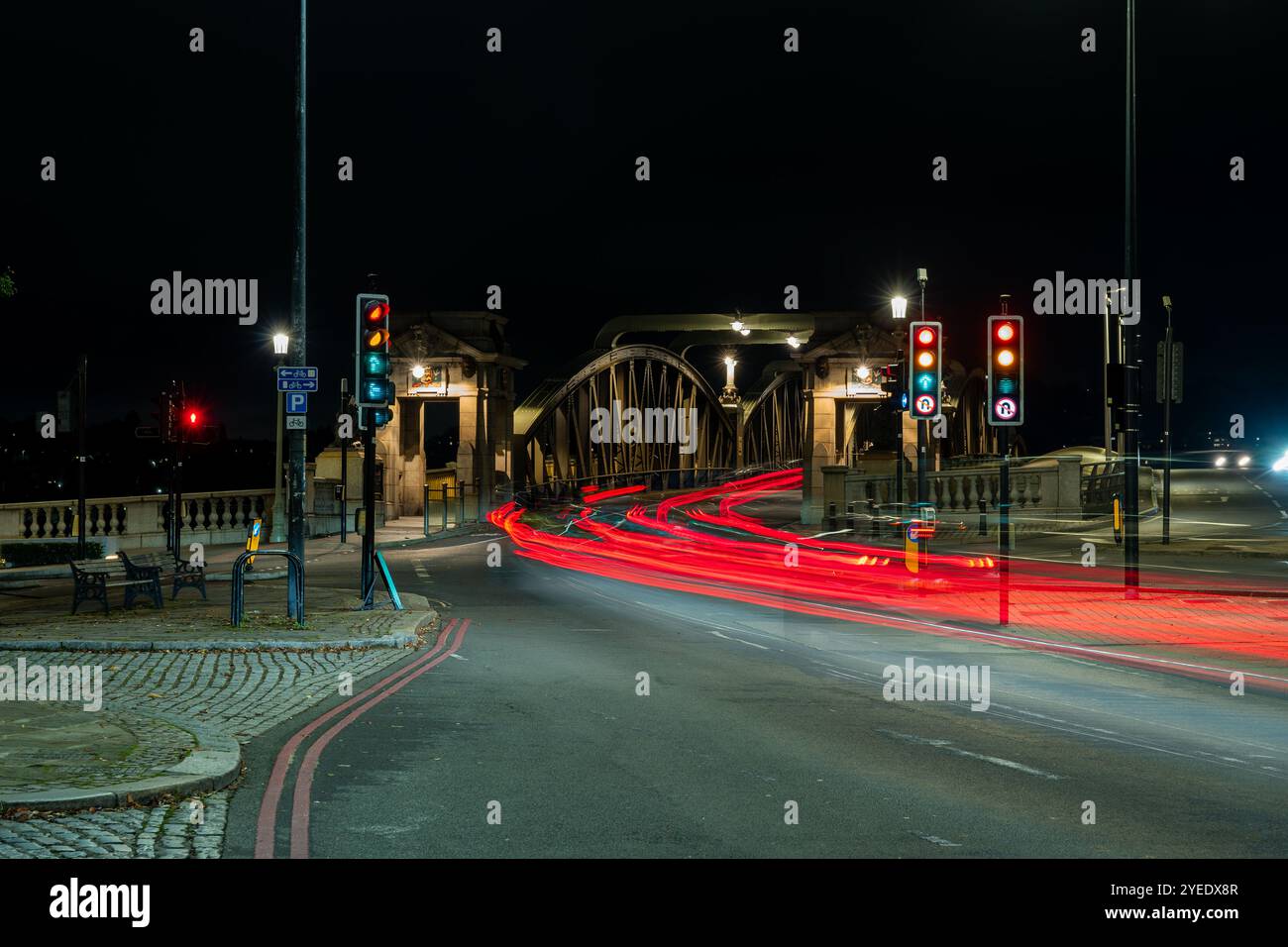 Red streaks of car lights illuminate a bridge at night, showcasing ...