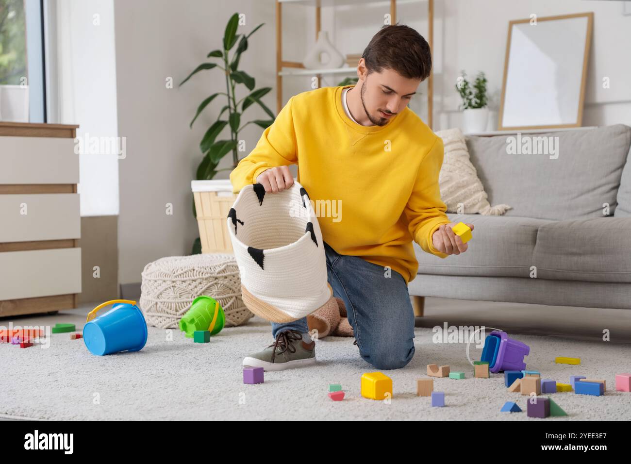 Stressed young father putting toys away in basket at home Stock Photo ...