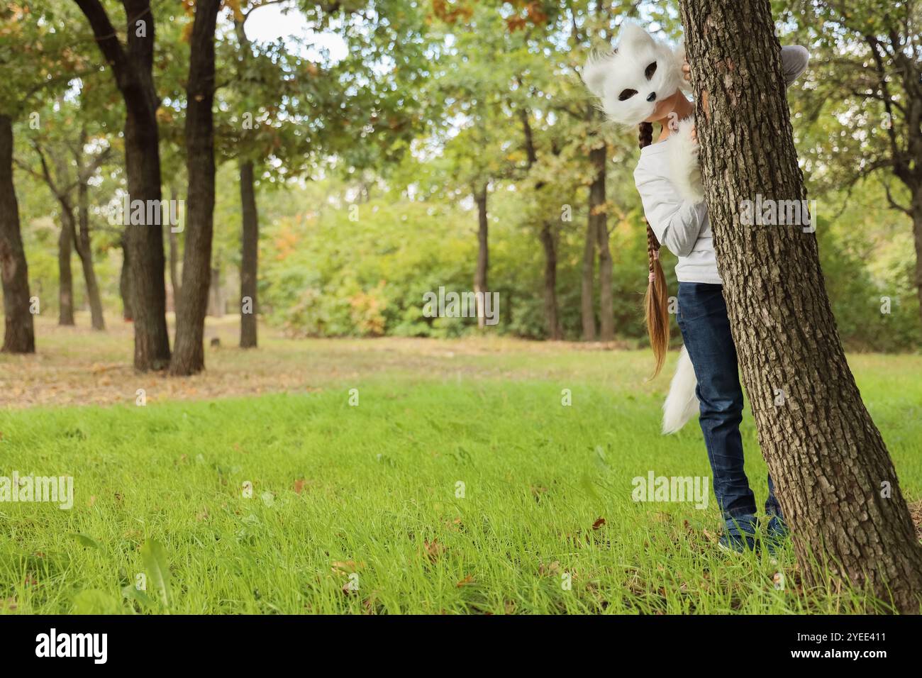 Quadrober girl with cat mask behind tree in park Stock Photo - Alamy