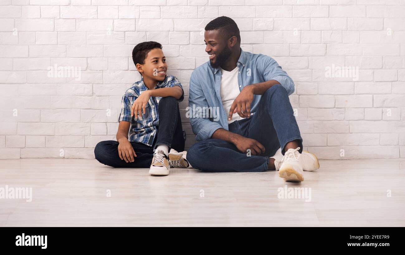 Happy Afro Dad And Son Sitting On Floor Against White Wall Stock Photo ...