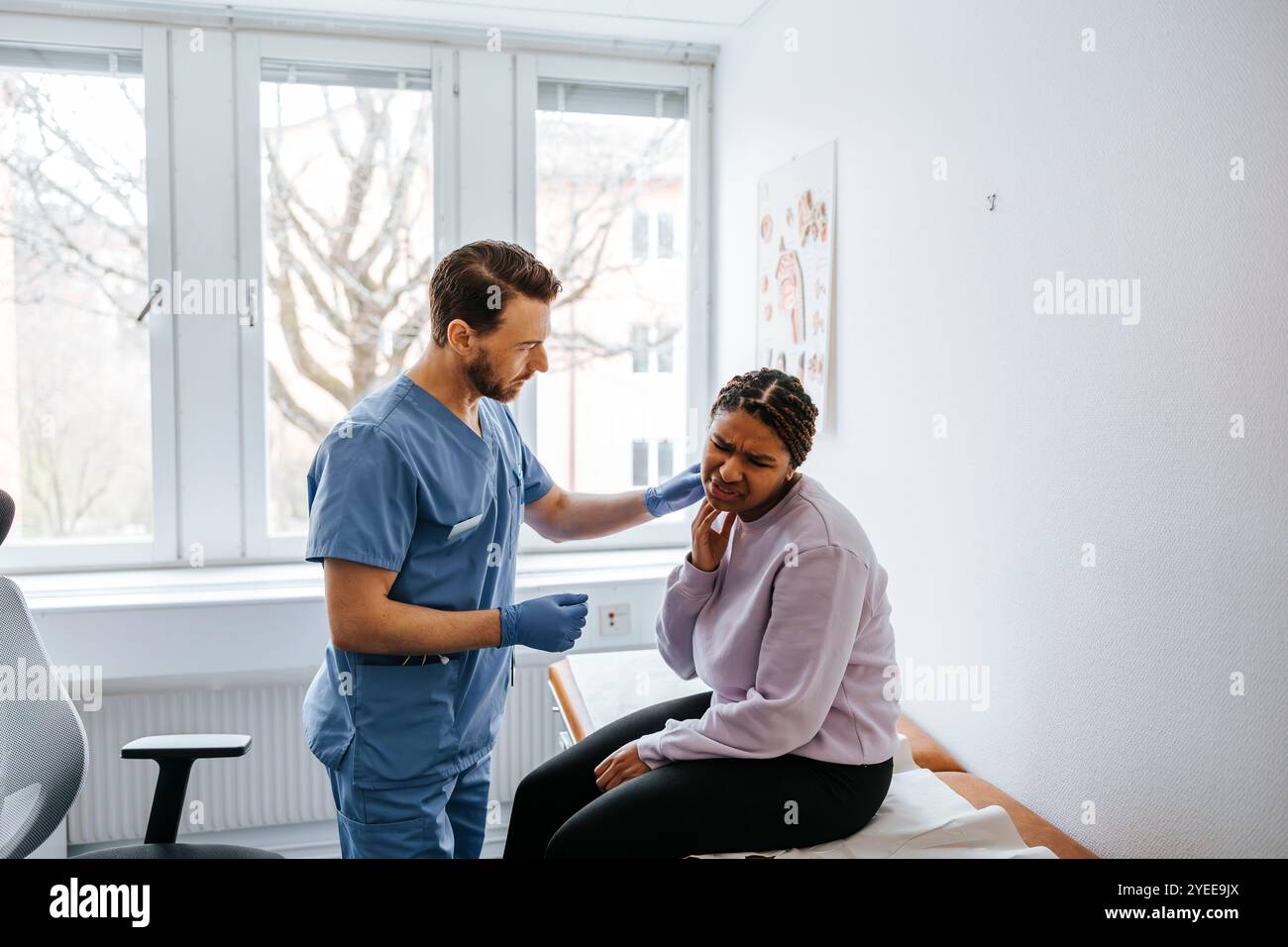 Male medical professional examining patient's neck ache while standing ...