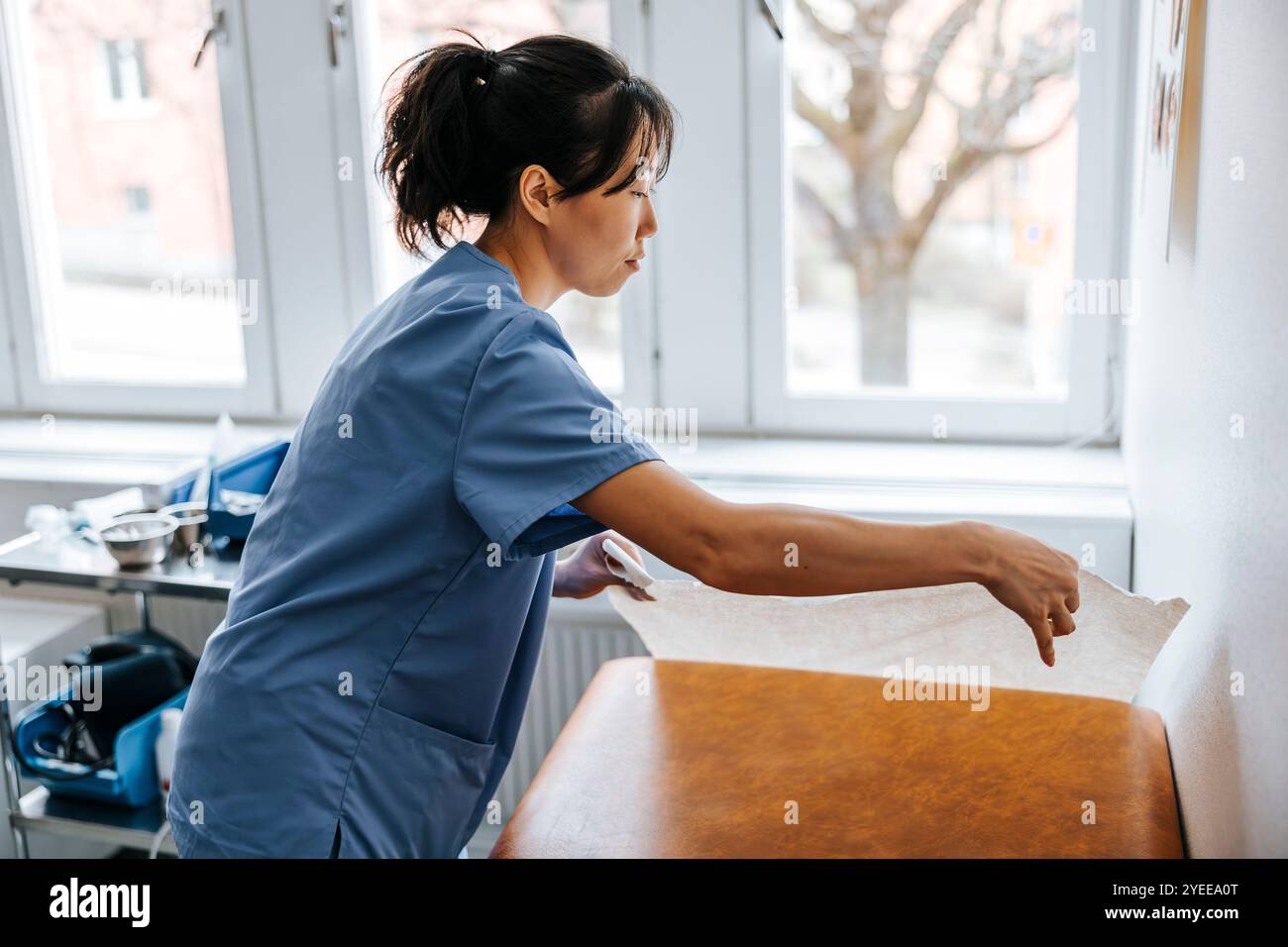 Side view of female healthcare worker putting sheet on bed in ...