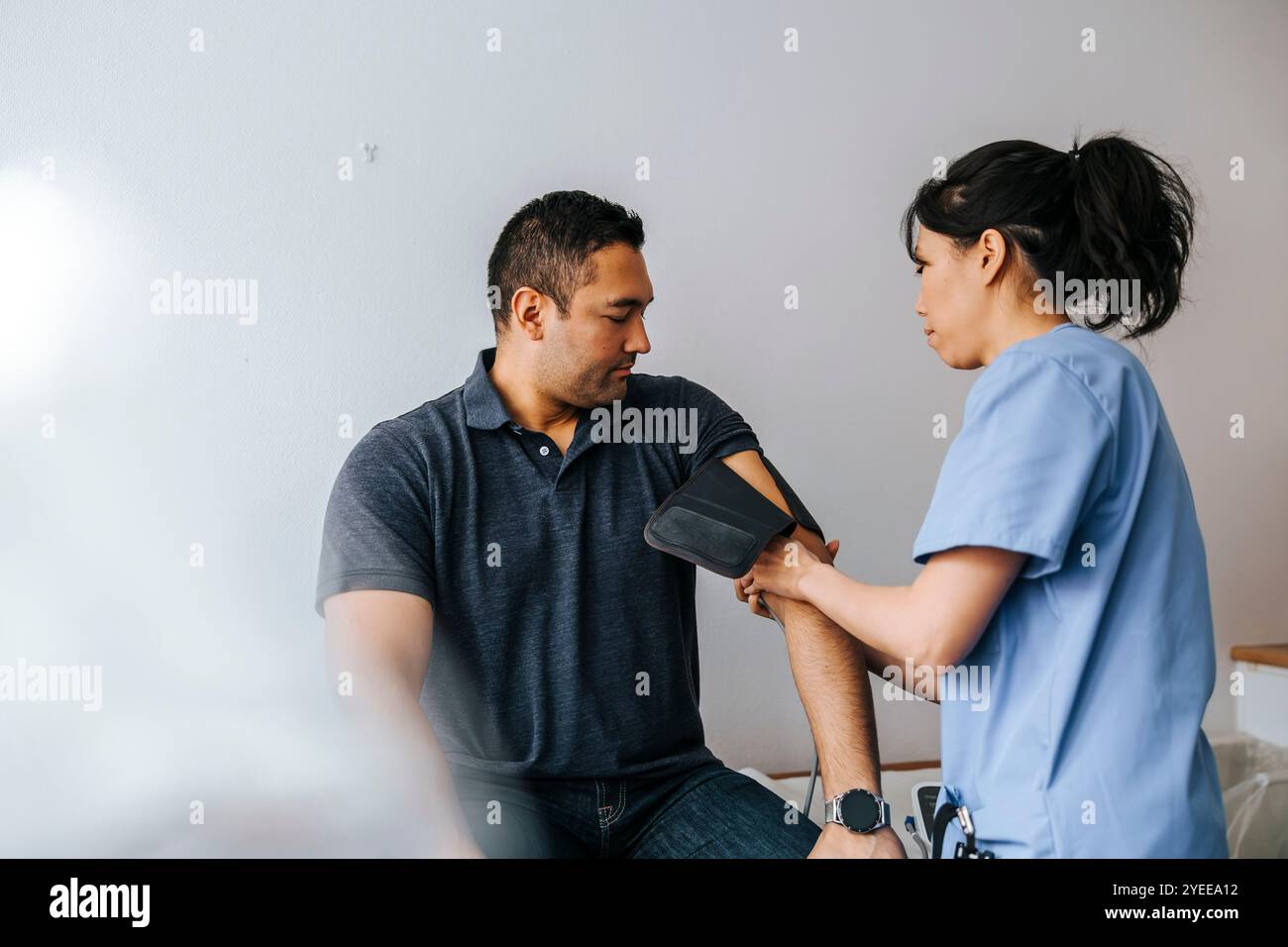 Female medical professional checking male patient's blood pressure in ...