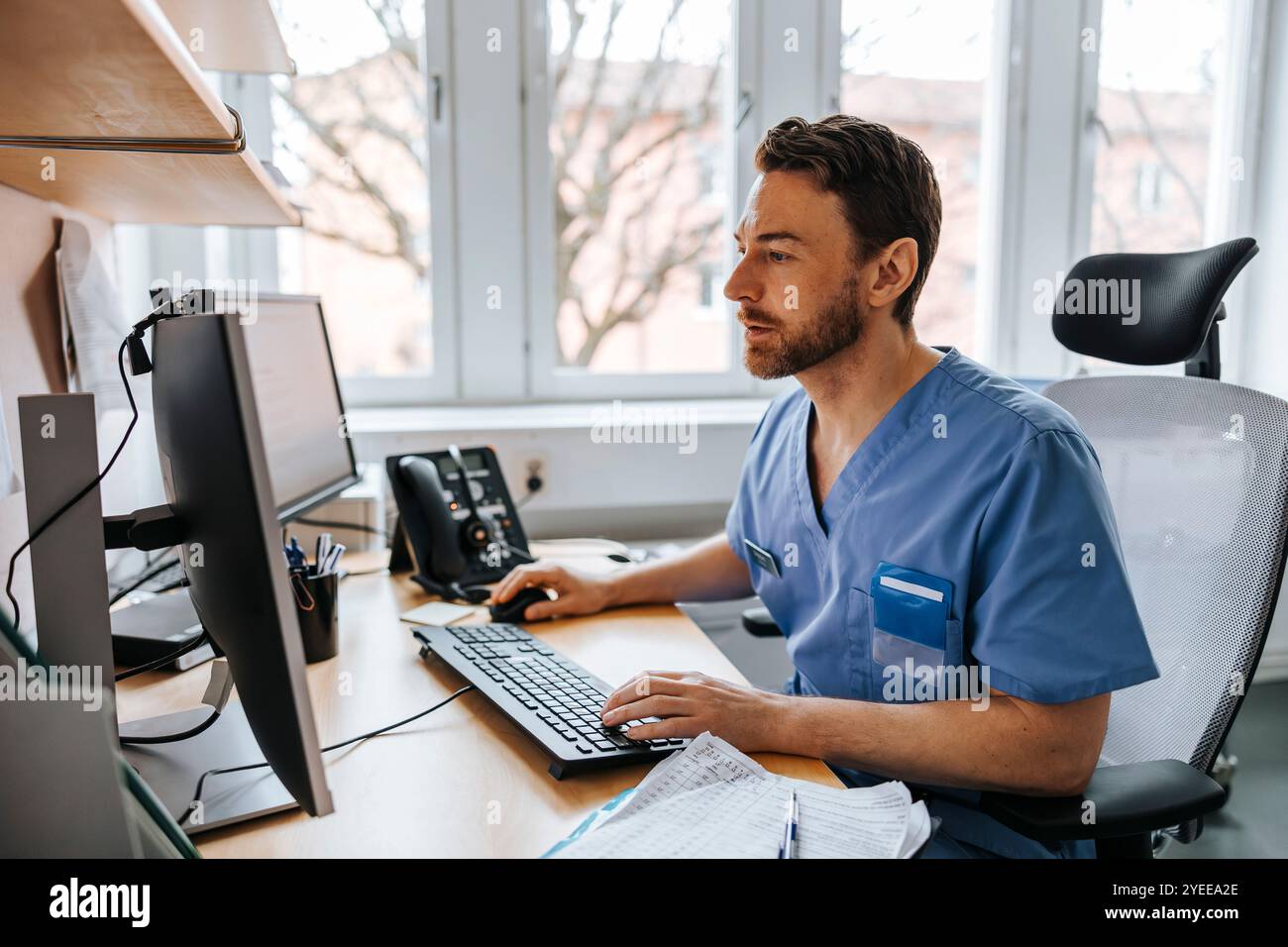 Focused male medical expert working on computer while sitting on chair ...