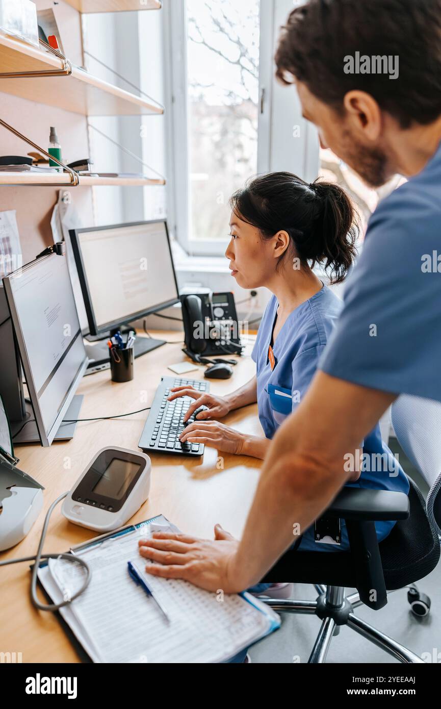 Focused female doctor typing on computer while working with coworker in ...