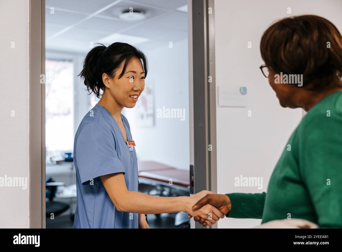 Smiling female medical professional greeting senior patient while ...