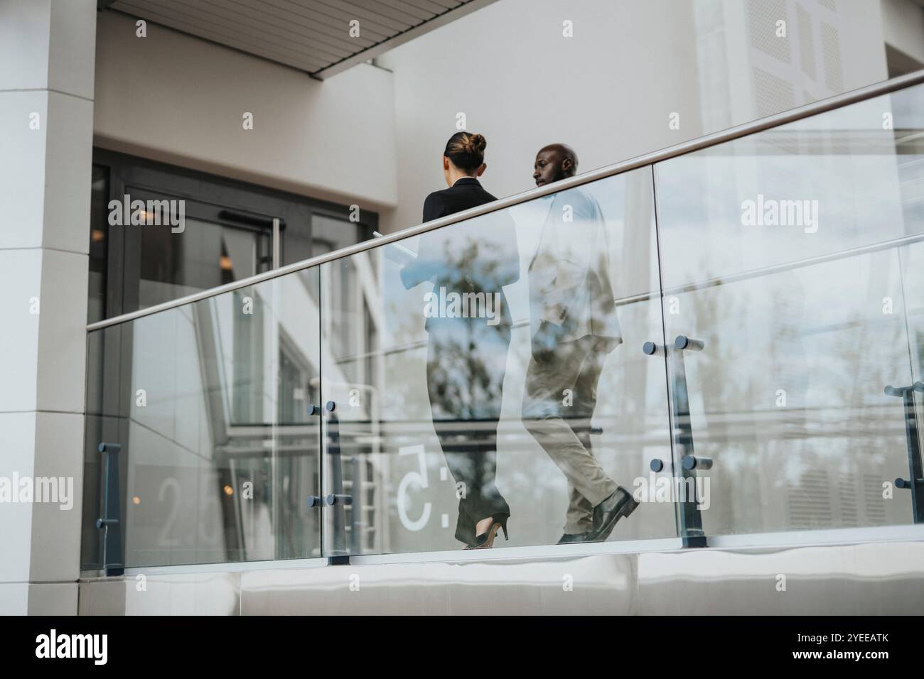 Full length of male and female colleagues walking by glass railing at ...