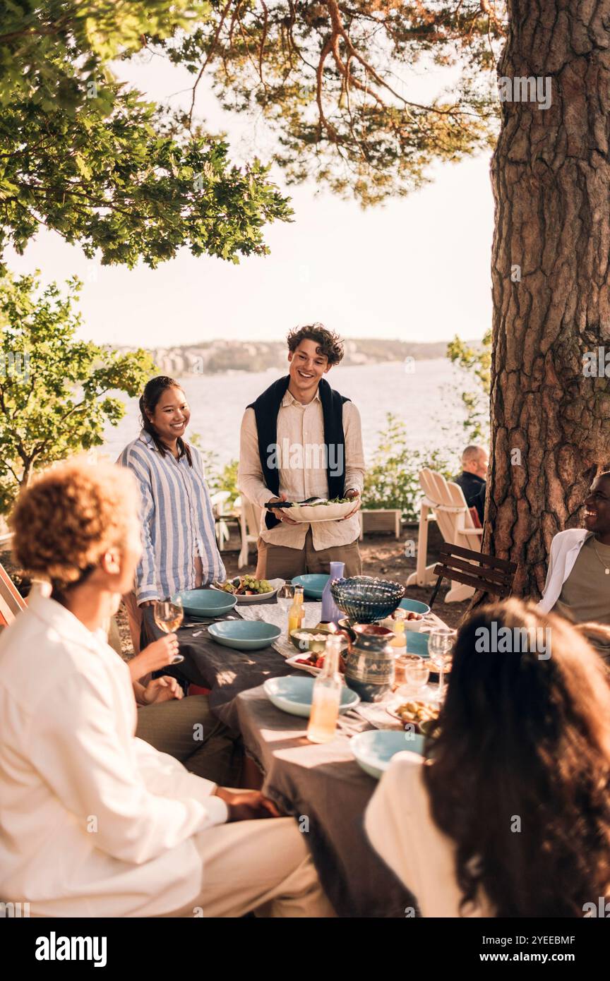 Smiling man holding food plate and talking with friends sitting at ...