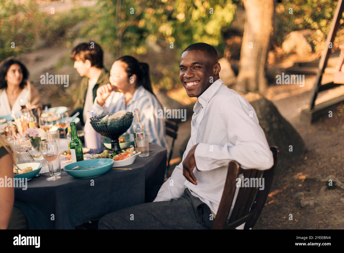 Side view of smiling man sitting on chair with friends at dining table ...