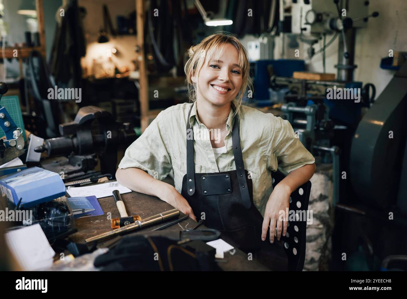 Portrait of smiling female craftsperson sitting on chair at workshop ...