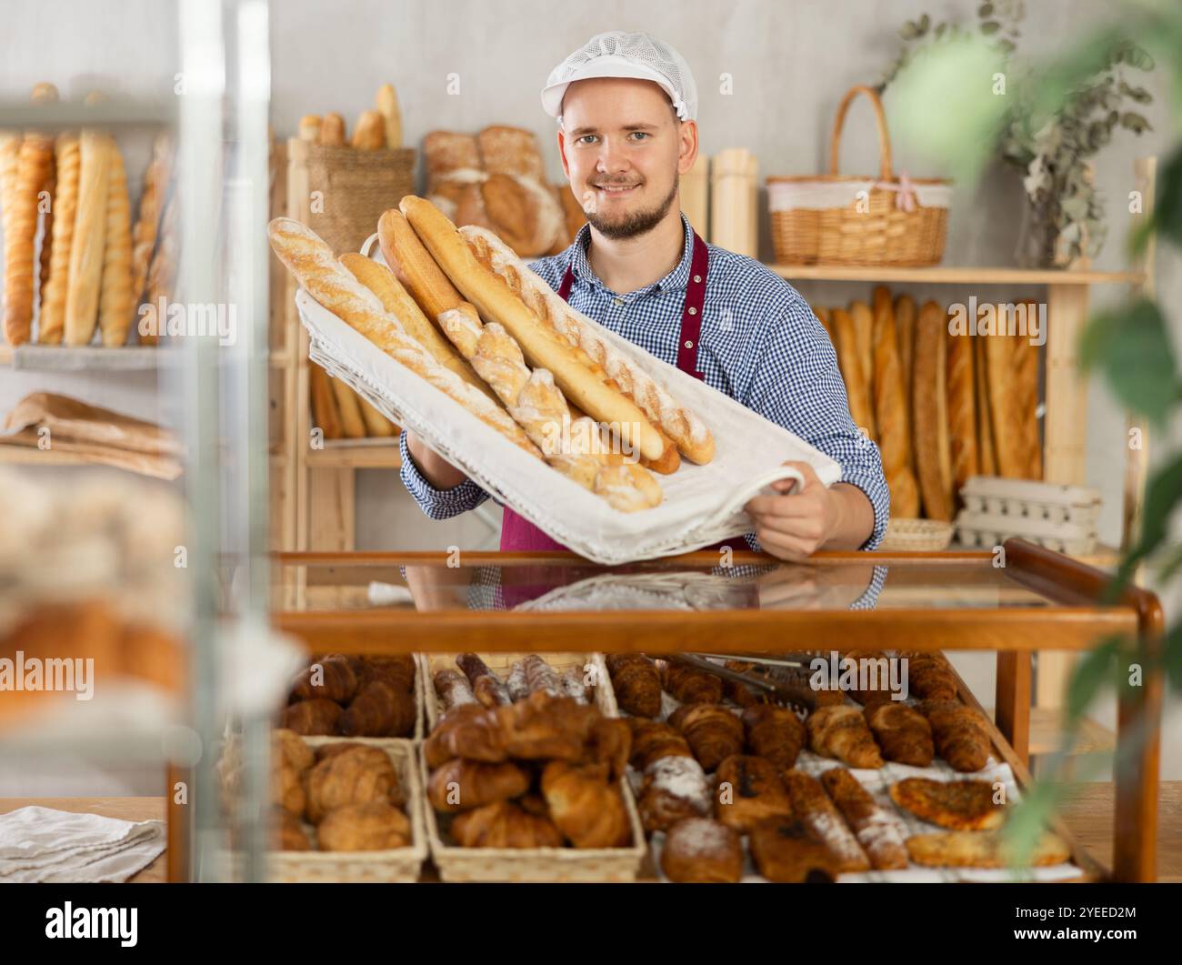 Male seller stands at bakery counter with basket filled by fresh ...