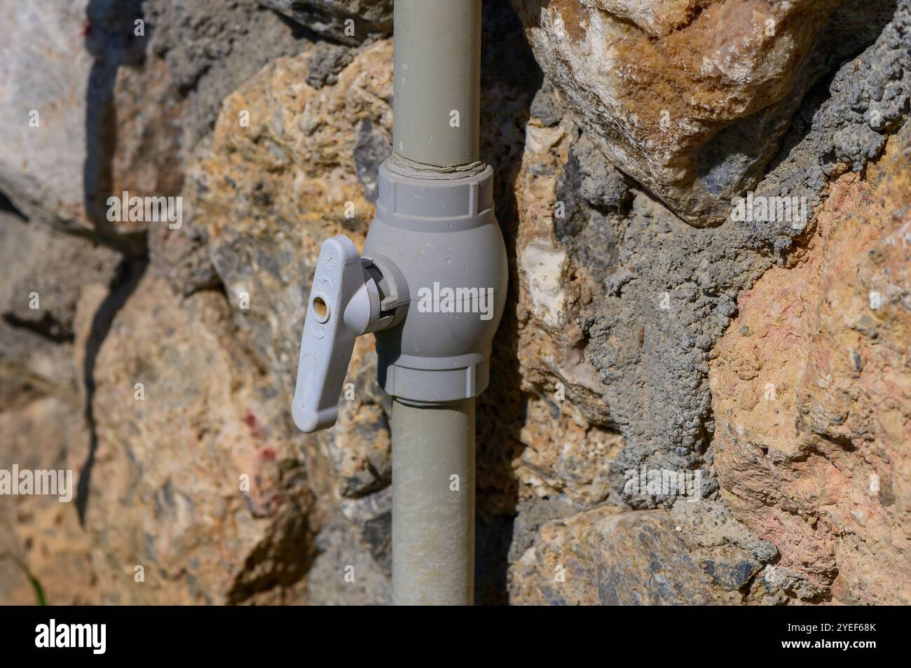 The gray valve blends into the rugged stone wall, showcasing industrial ...