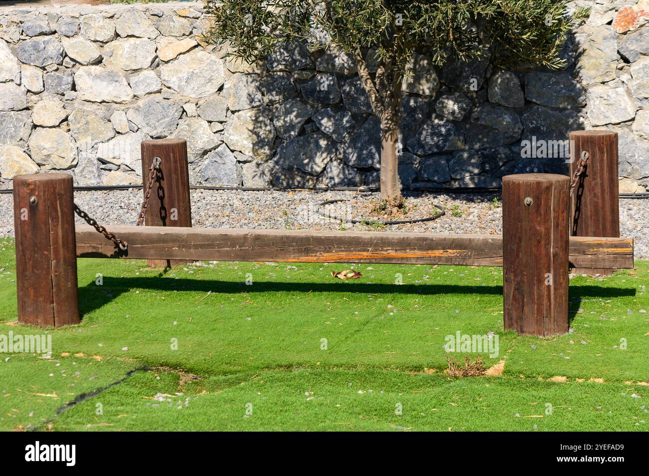 A wooden balancing beam with chains rests on green grass, framed by a ...