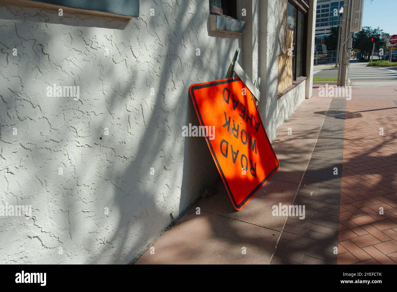 Orange Road Work Ahead sign on brick sidewalk leaning up beside a gray ...