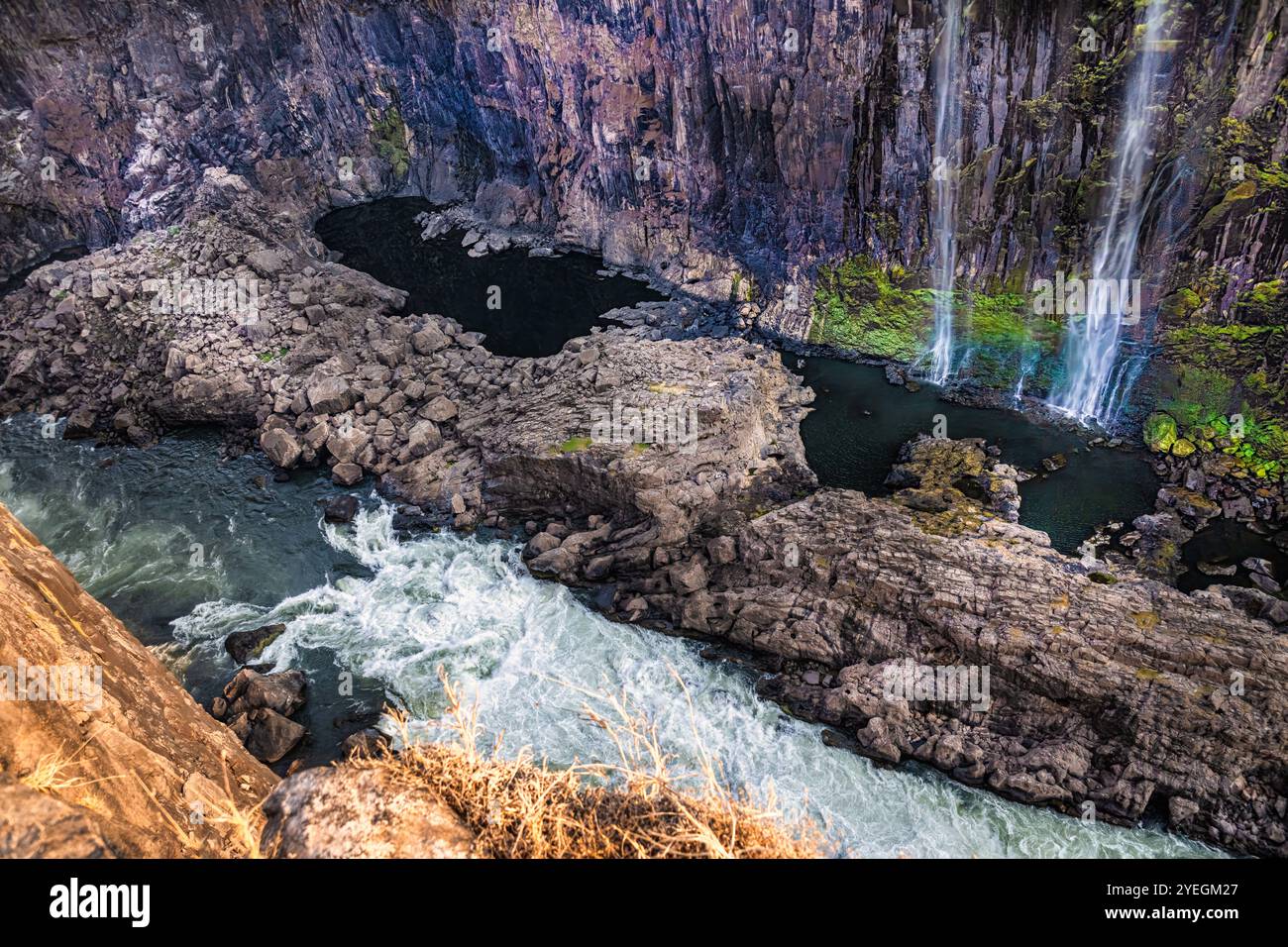 A gushing river flows energetically beneath towering cliffs, creating a ...