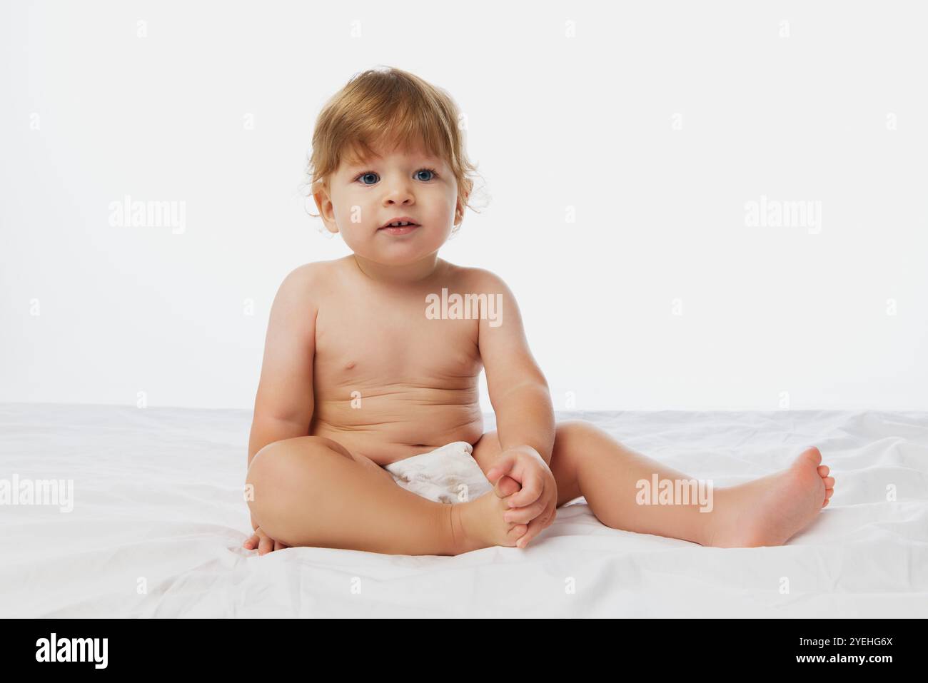 Baby, little toddler in diaper sitting with crossed legs, holding foot ...