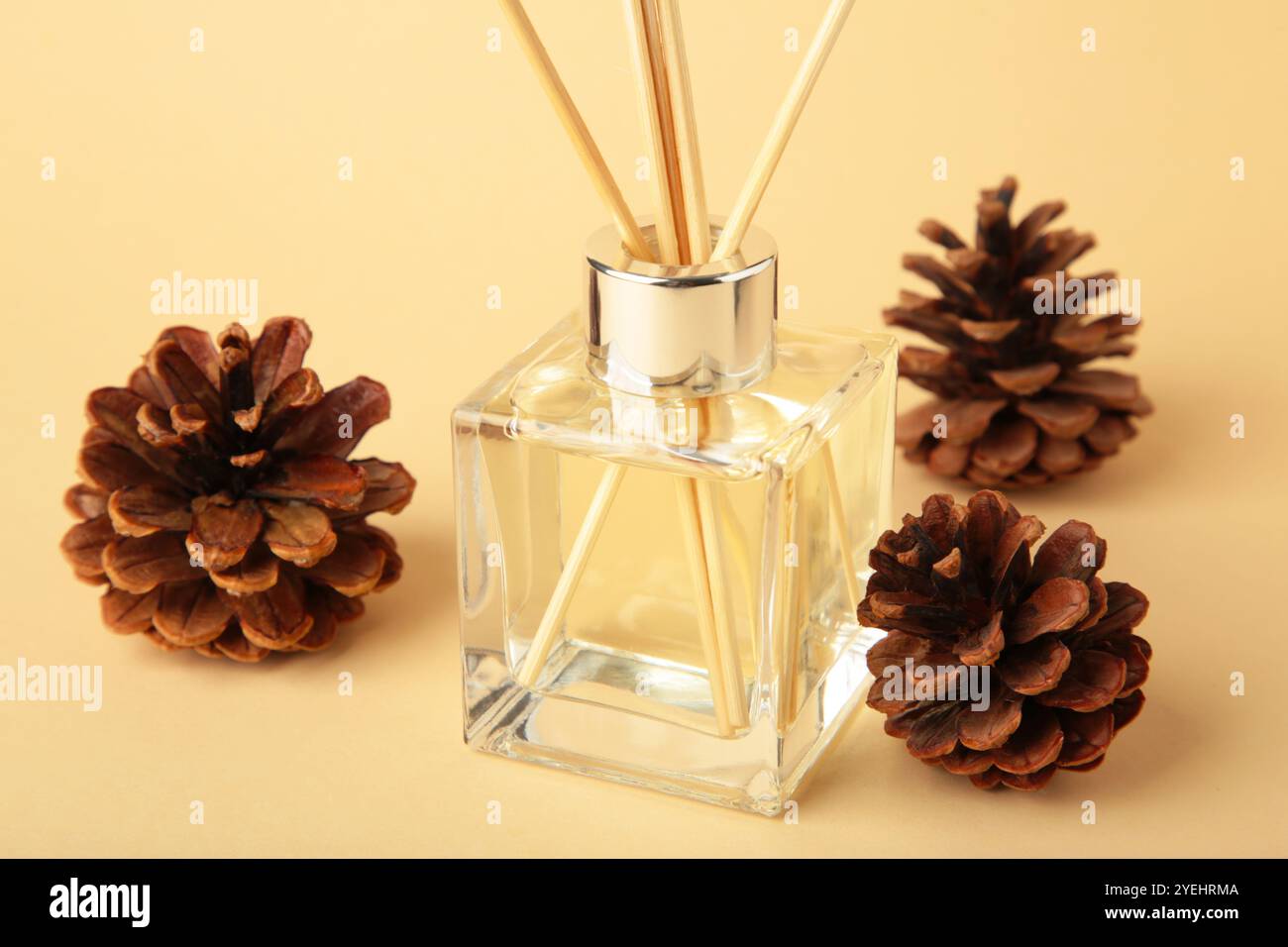 Glass bottle of aroma diffuser and pine cones on beige background. Top ...