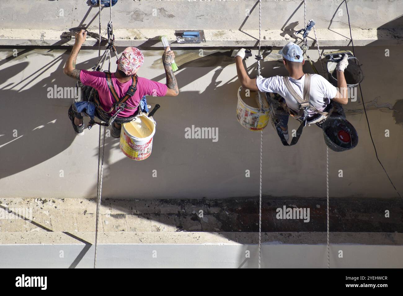 Painter hanging from a rope while working on a facade, symbolic image ...