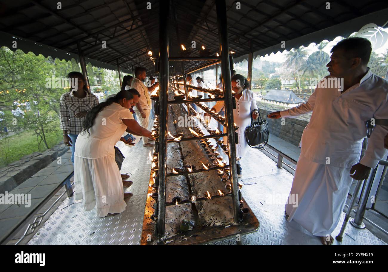 Sri Lankan pilgrims pour oil into candle holders at the Buddhist Temple ...