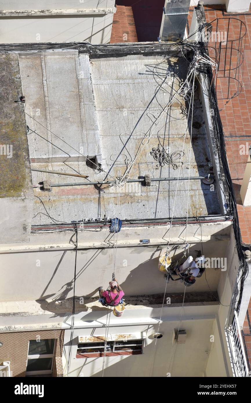 Painter hanging from a rope while working on a facade, symbolic image ...
