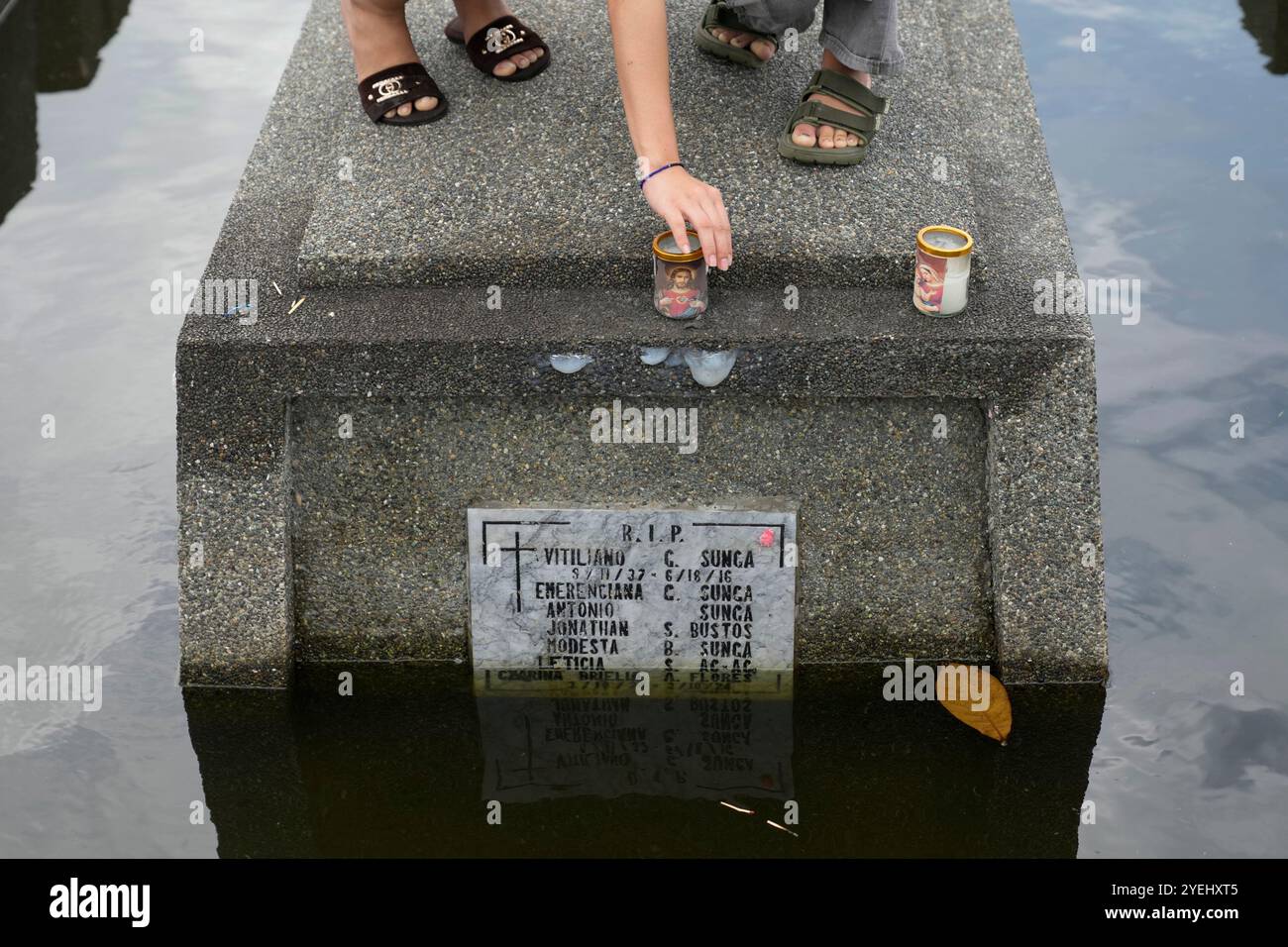 A woman covers candles placed on the half-submerged tomb of family ...
