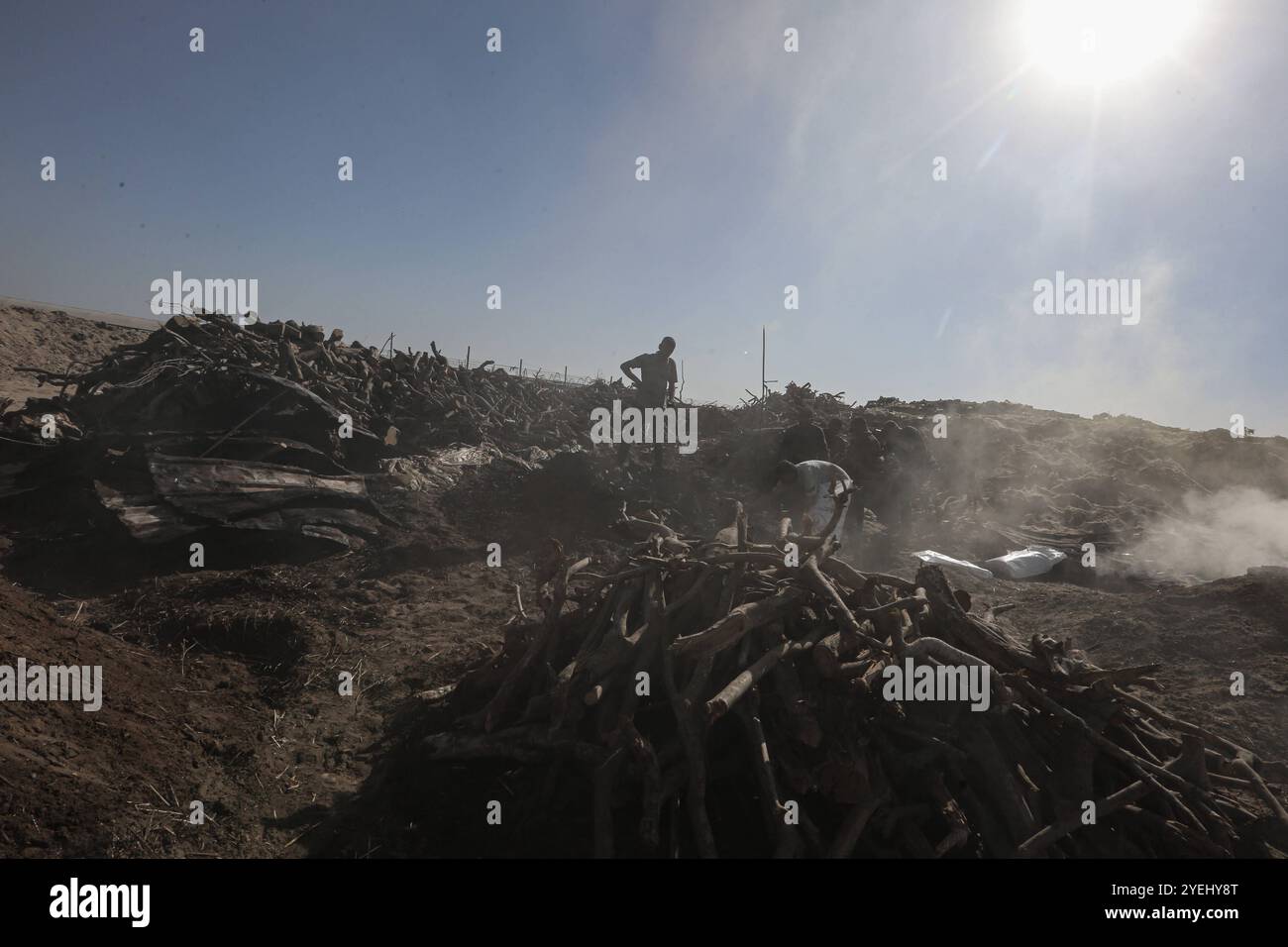 Palestinian workers rakes burnt wood at a charcoal production site in ...