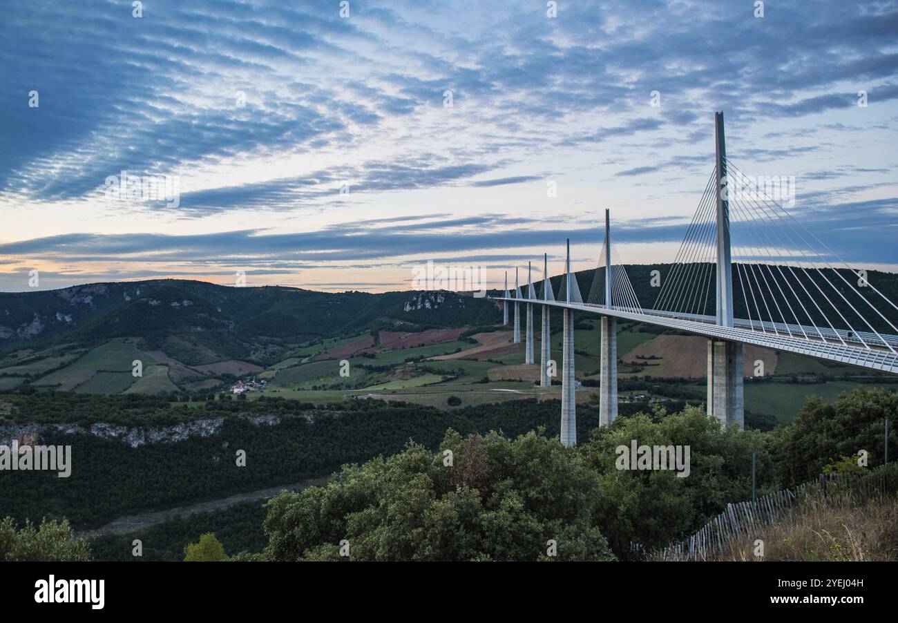 A suspension bridge stretches across a lush valley under a sky filled ...