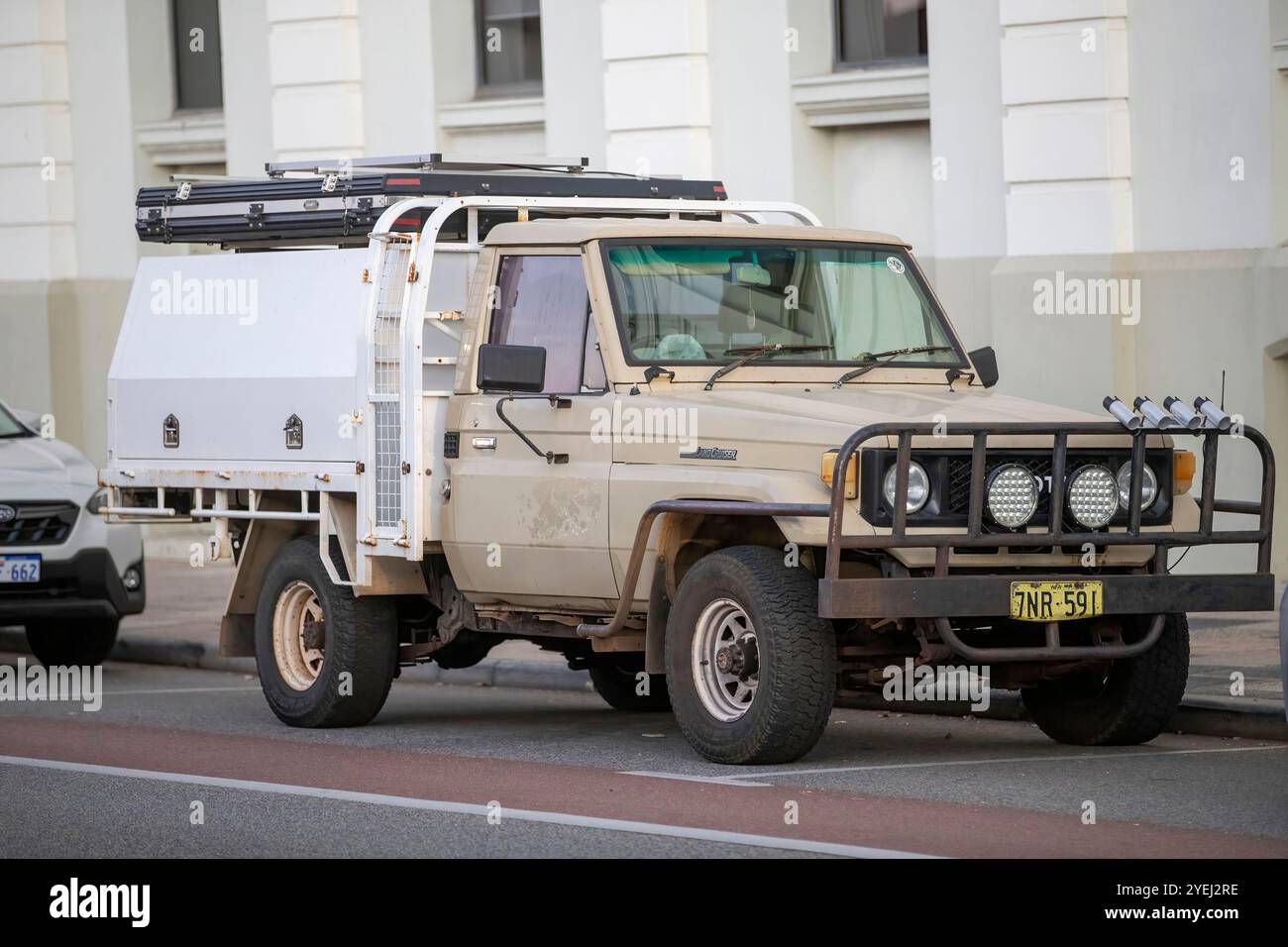 The image features a beige Toyota Land Cruiser parked on the street ...