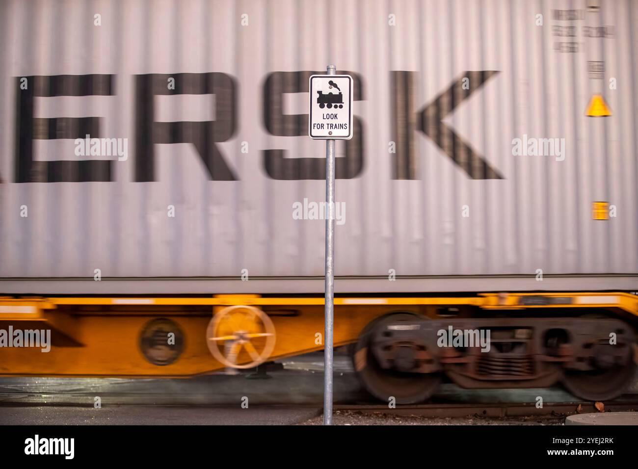 This photograph captures a "Look for Trains" sign in sharp focus with a ...