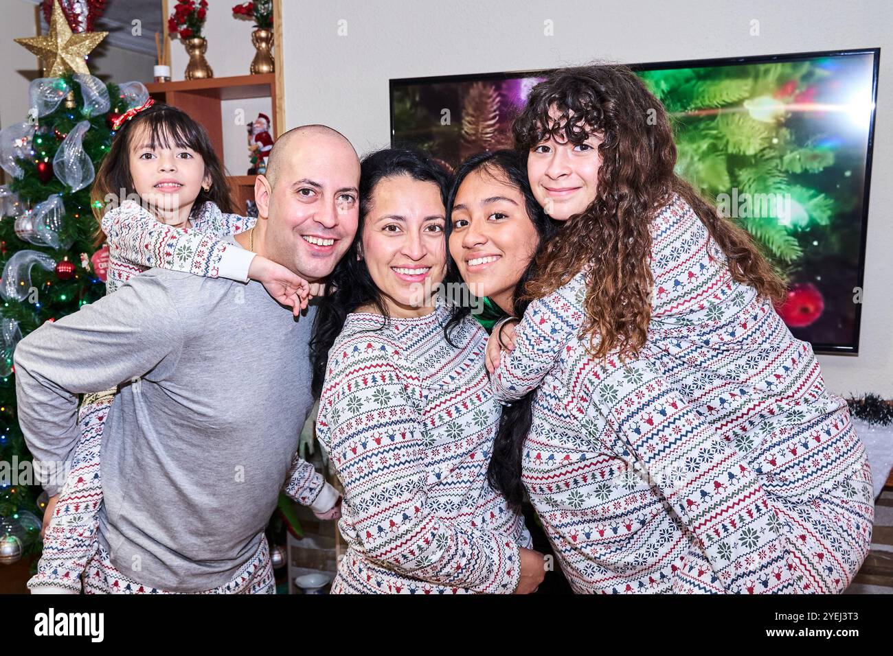 A family of four in pajamas poses for a picture in front of a Christmas ...