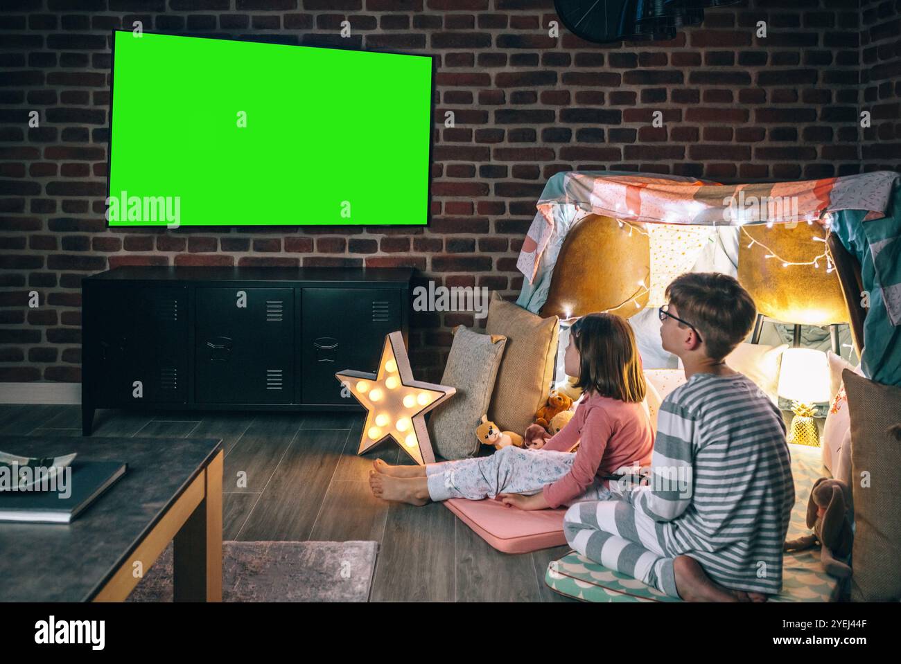 Two concentrated children sitting over mats while watching television ...