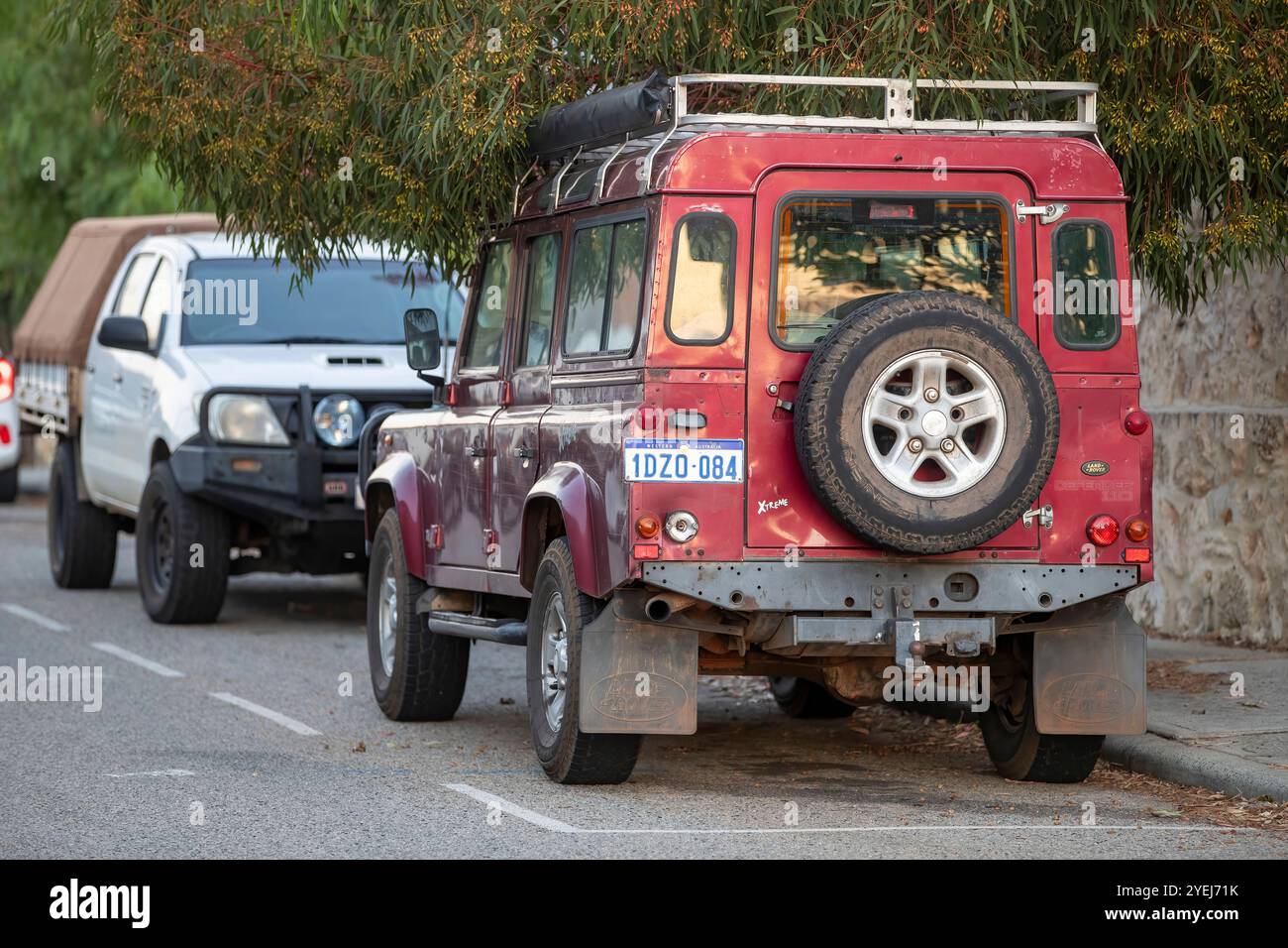 A red Land Rover Defender with a roof rack and spare tire mounted on ...