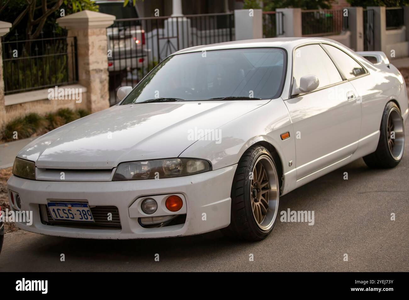 white Nissan Skyline parked on a suburban street, featuring aftermarket ...