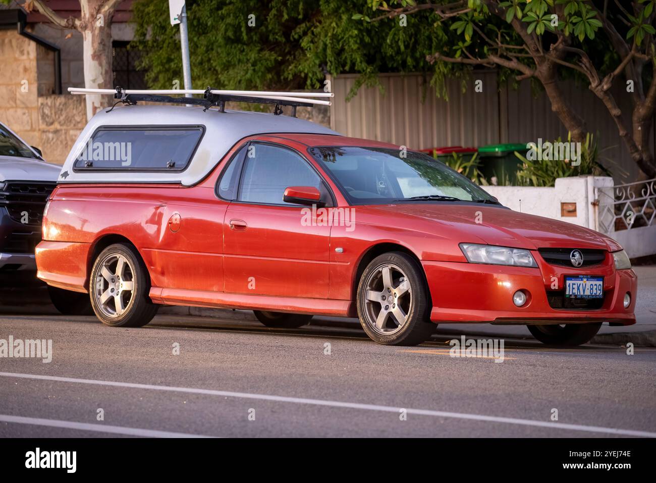 A red Holden ute parked on a suburban street, featuring a silver canopy ...