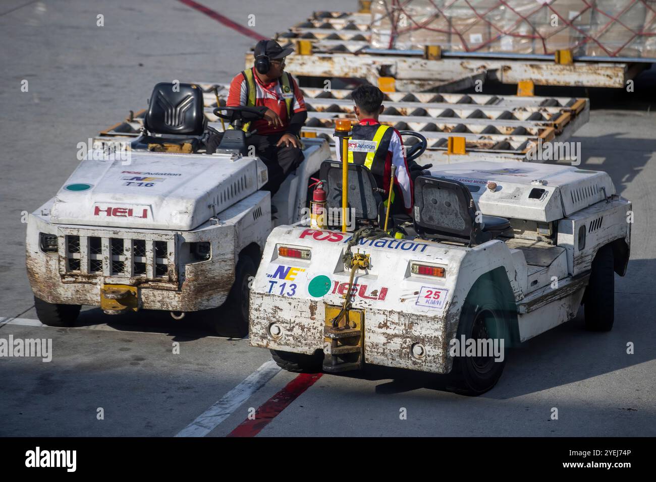 Two ground crew members operate airport baggage towing vehicles ...