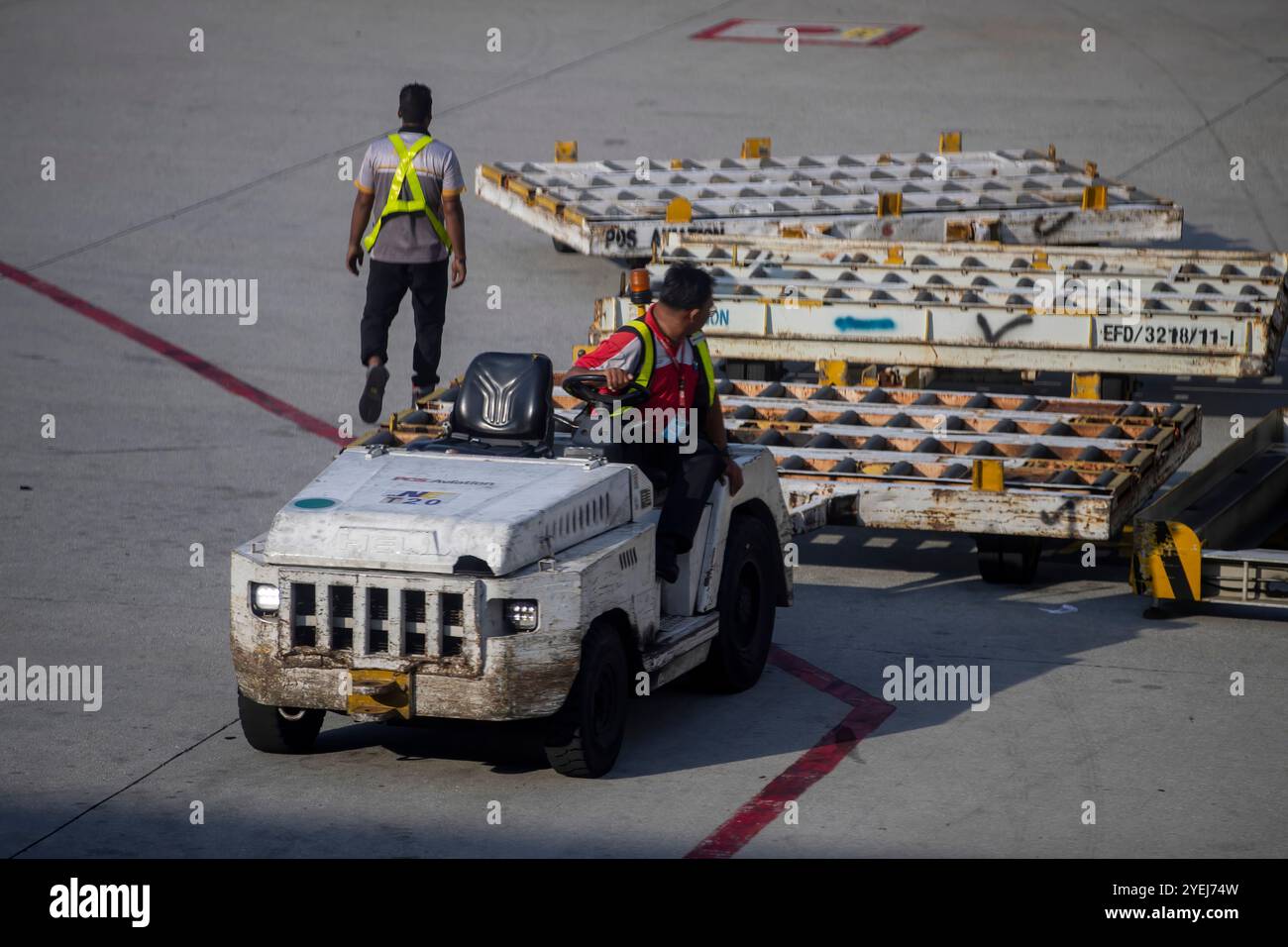 Ground crew member driving a baggage towing vehicle while another ...